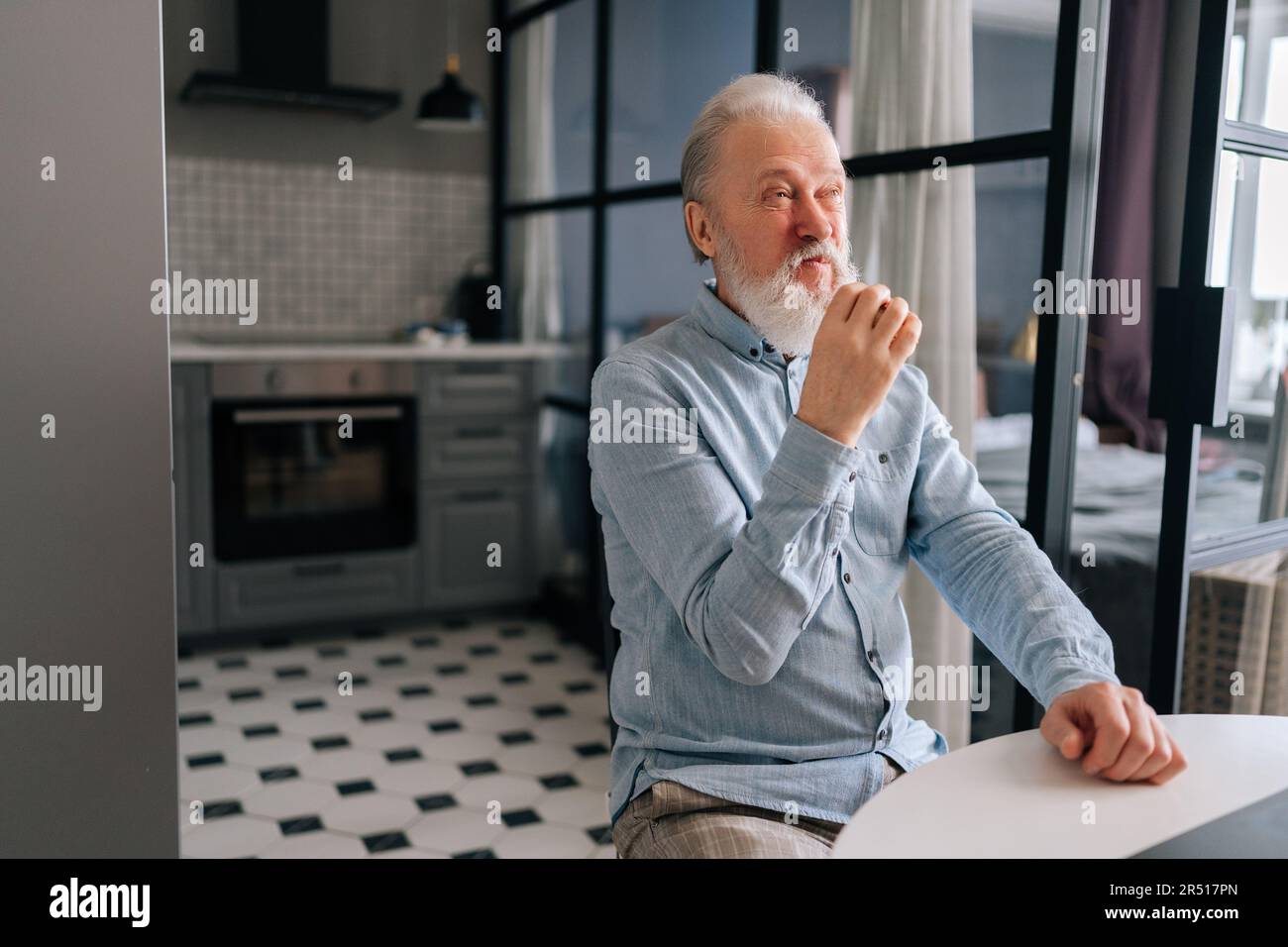 Disgruntled mature adult male eating unappetizing burger at kitchen ...