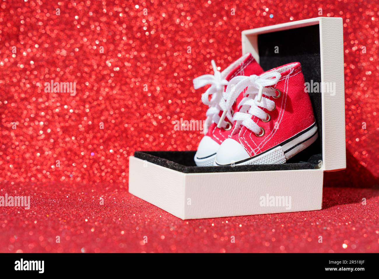 Pair of tiny red high-top canvas shoes placed in a small gift box ...