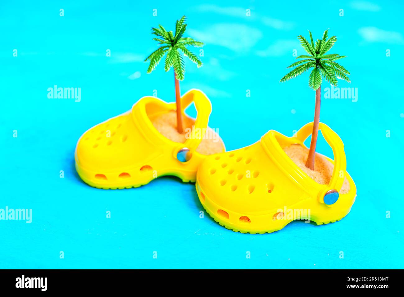 Yellow clogs with sand and toy palm trees isolated on a blue background ...