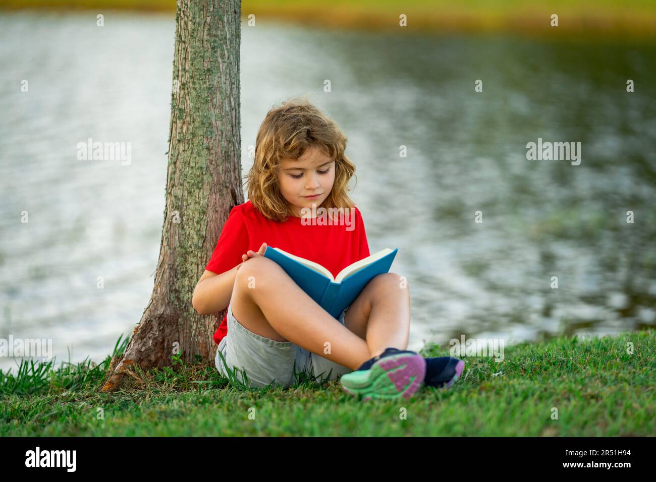 Cute kid reading book on meadow outdoors. School and education. Nature ...