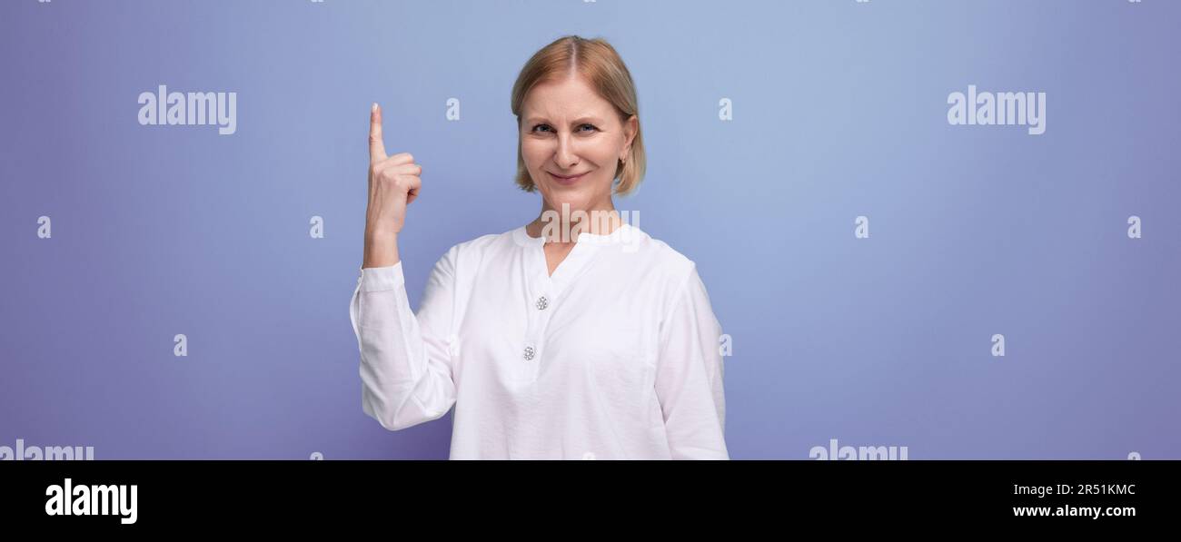pretty blonde 50s woman in white blouse pointing her finger to the side ...