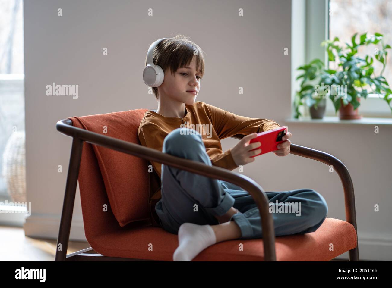 Relaxed child boy in headphones sits on armchair using phone as game ...