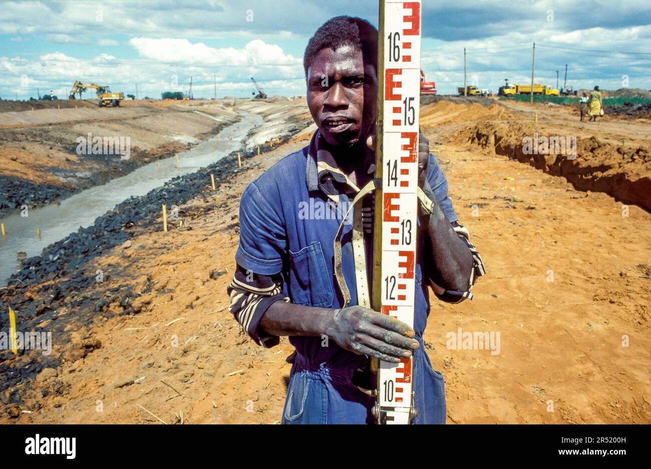 Mozambique, Maputo; A man is surveying land while construction workers ...