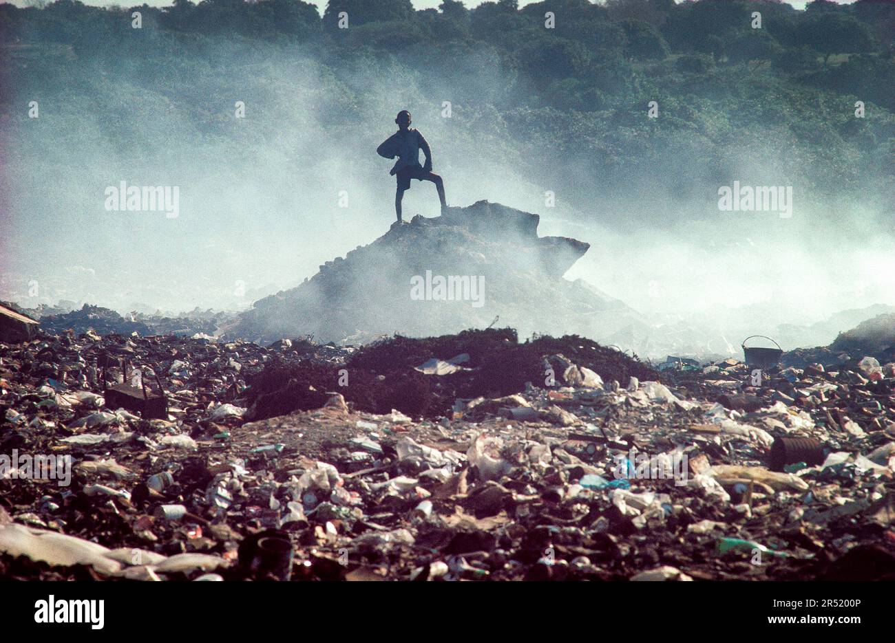 Mozambique, Maputo; Boy standing on top of a garbage dump, surrounded ...