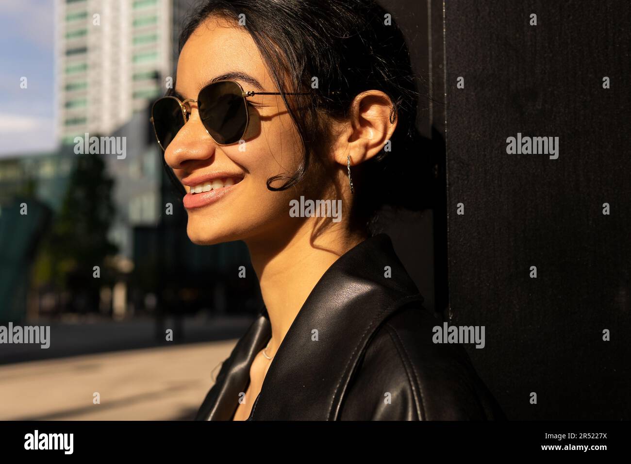 Side view of happy young woman in leather jacket and sunglasses by a ...