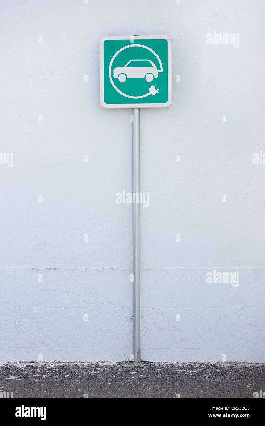 Signpost with symbol of electric car on ground near white wall on ...