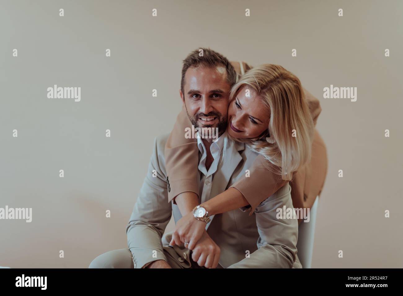 A business couple posing for a photograph together against a beige ...