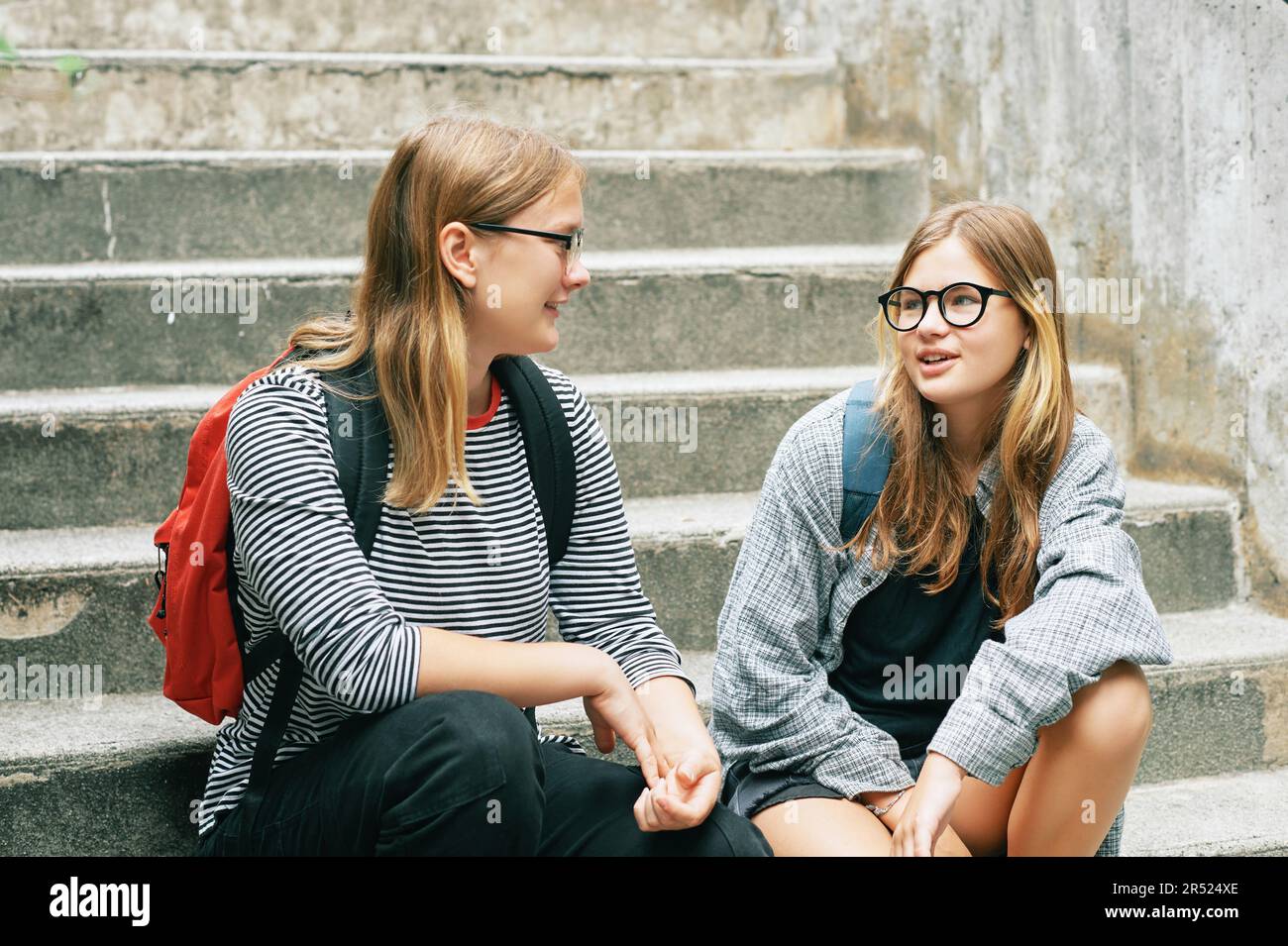 Outdoor portrait of two teenage girl sitting on stairs, wearing ...