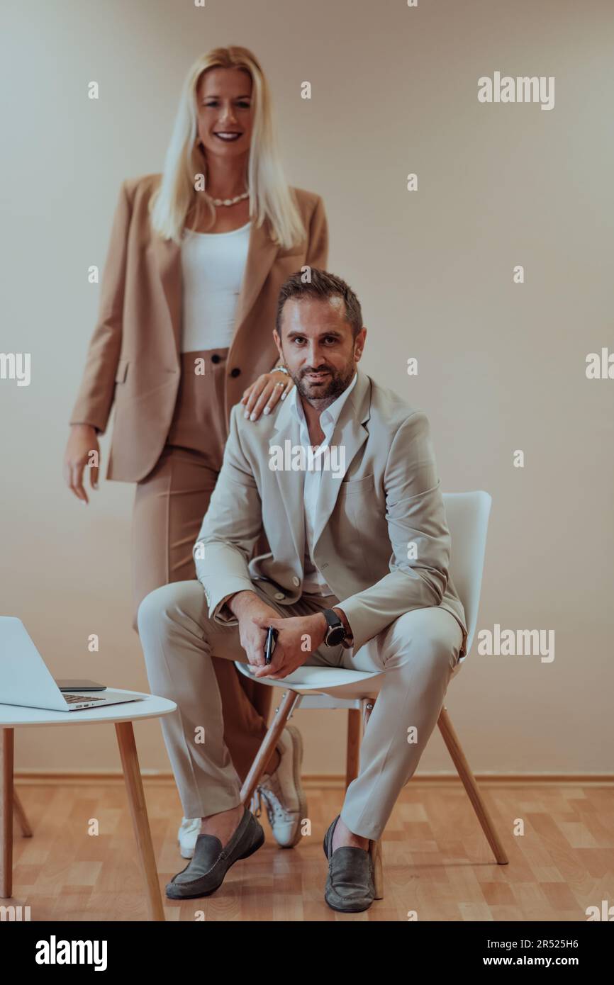 A business couple posing for a photograph together against a beige ...