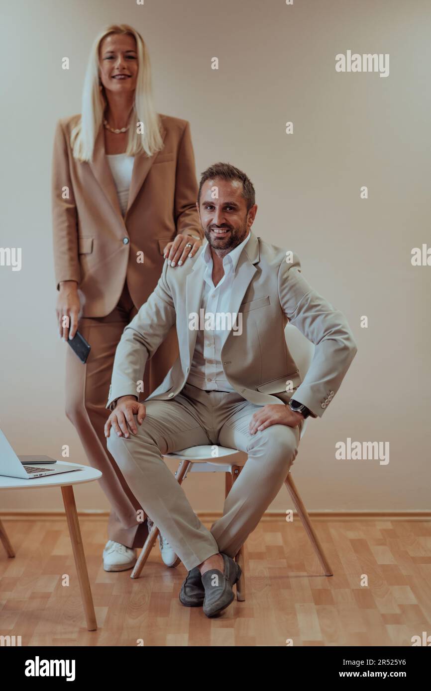 A business couple posing for a photograph together against a beige ...
