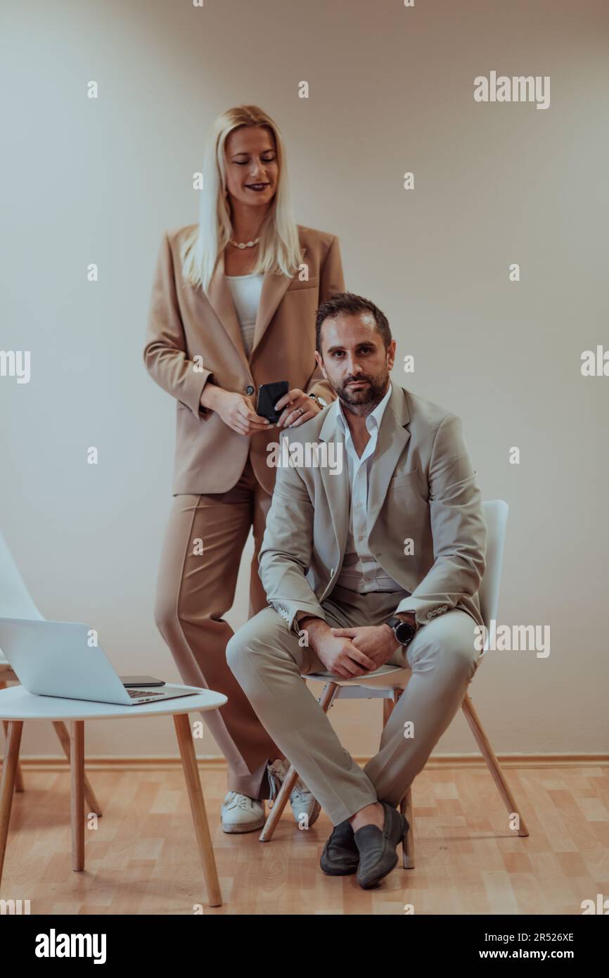 A business couple posing for a photograph together against a beige ...