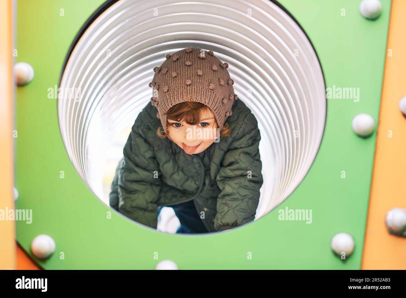 Cute toddler girl having fun on playground, crawling through tube, cold ...