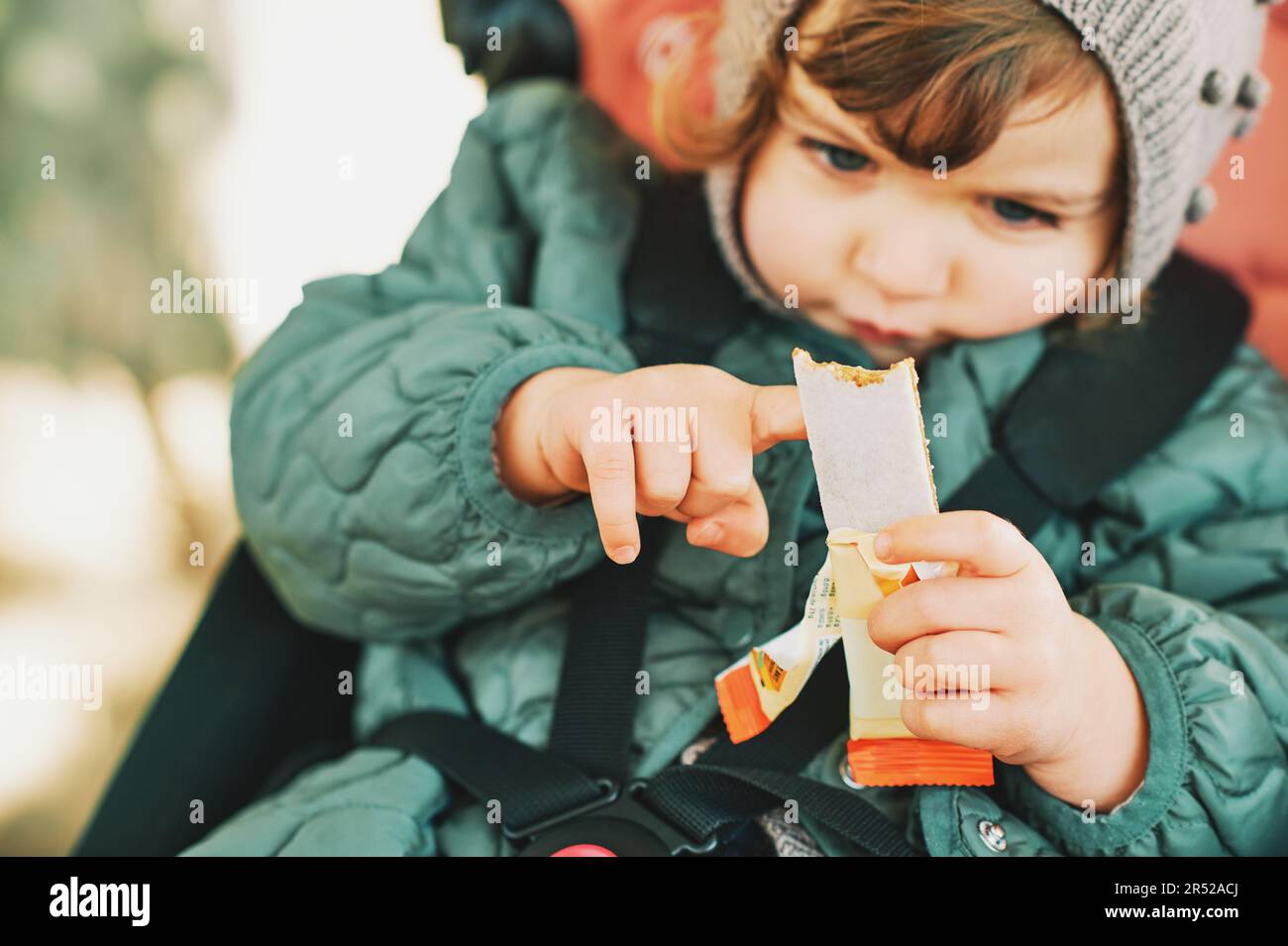 Happy toddler kid eating fruit bar, healthy snack, sitting in stroller ...
