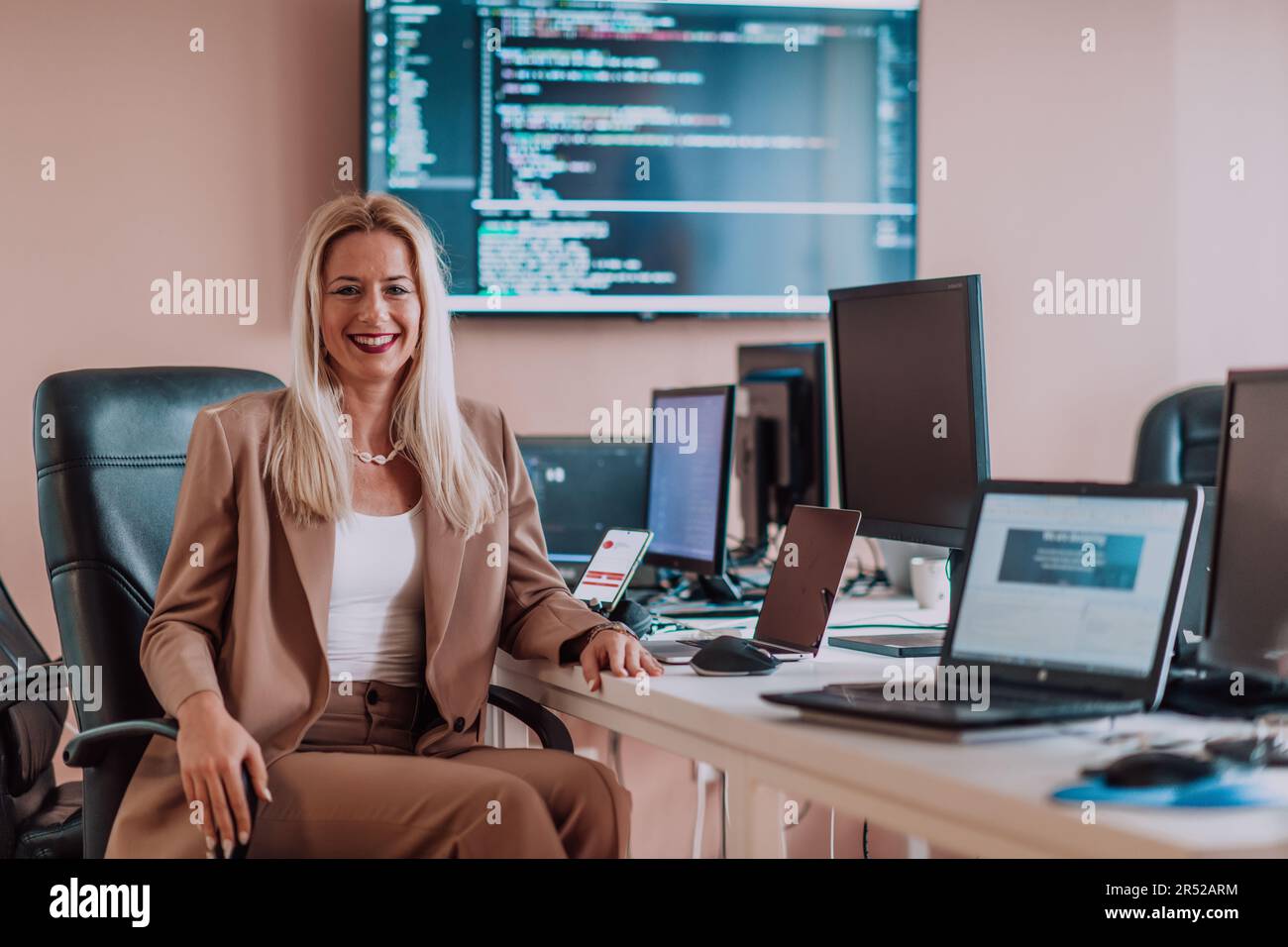 A businesswoman sitting in a programmer's office surrounded by computers, showing her expertise ...