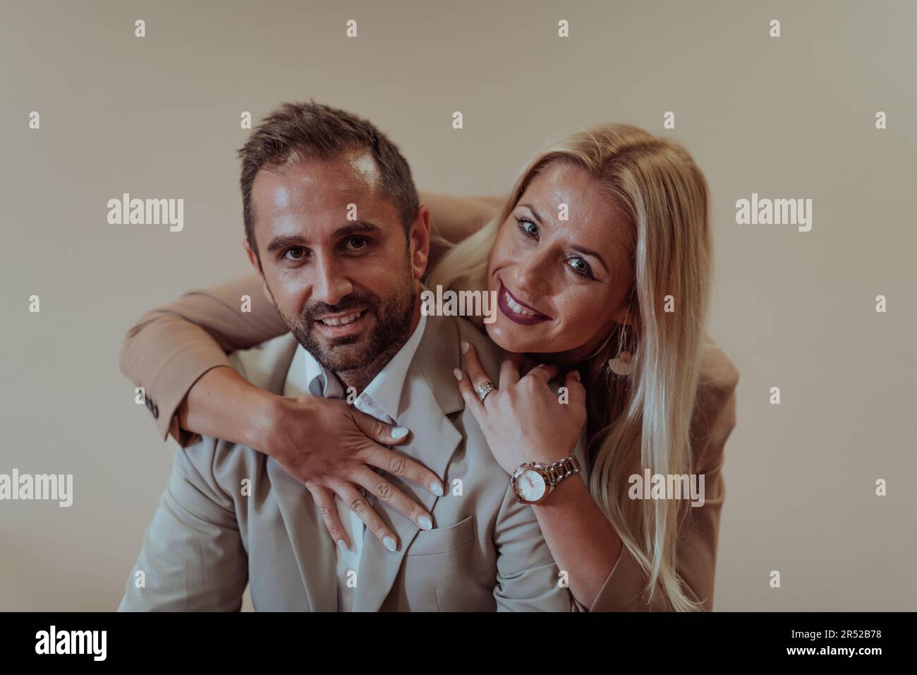 A business couple posing for a photograph together against a beige ...