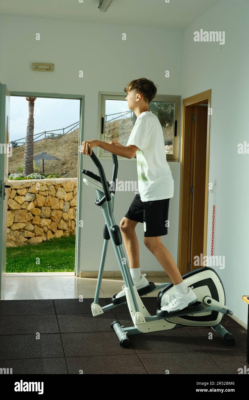 Teenage boy using elliptical training machine at apartment and ...