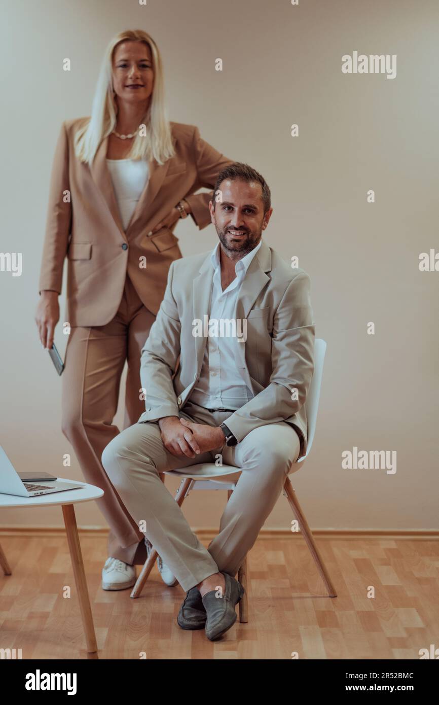 A business couple posing for a photograph together against a beige ...