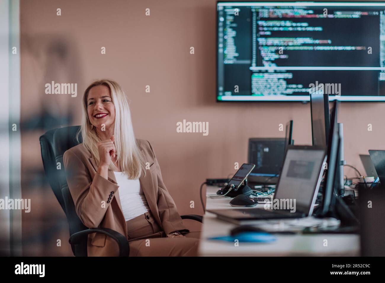 A businesswoman sitting in a programmer's office surrounded by computers, showing her expertise ...