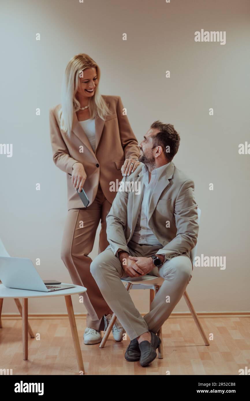A business couple posing for a photograph together against a beige ...