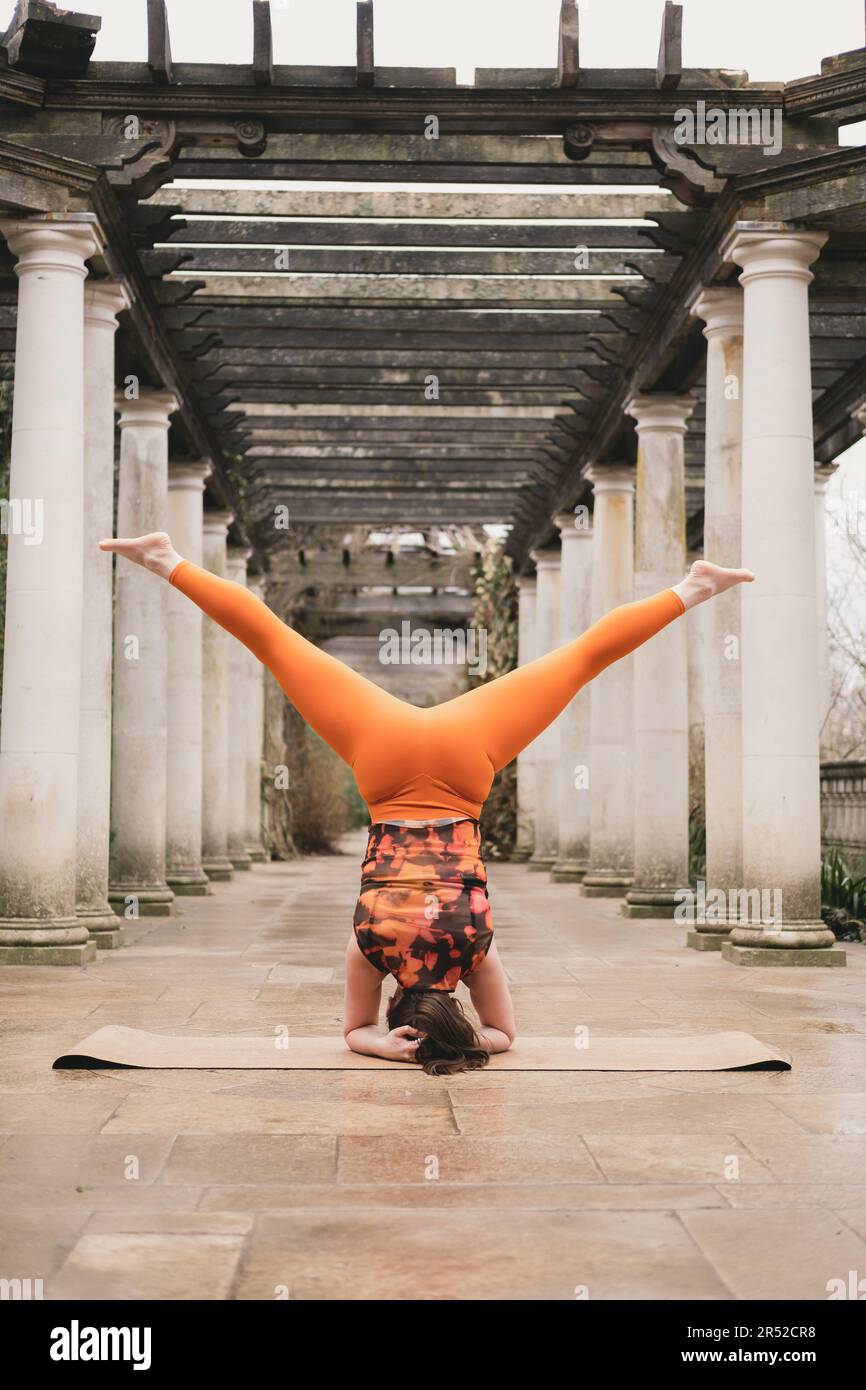 Rear view of woman doing a headstand wide legs pose in the terrace of a ...