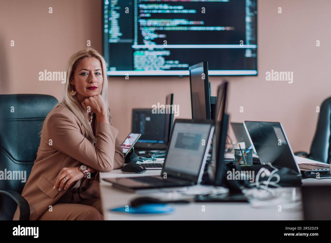 A businesswoman sitting in a programmer's office surrounded by computers, showing her expertise ...