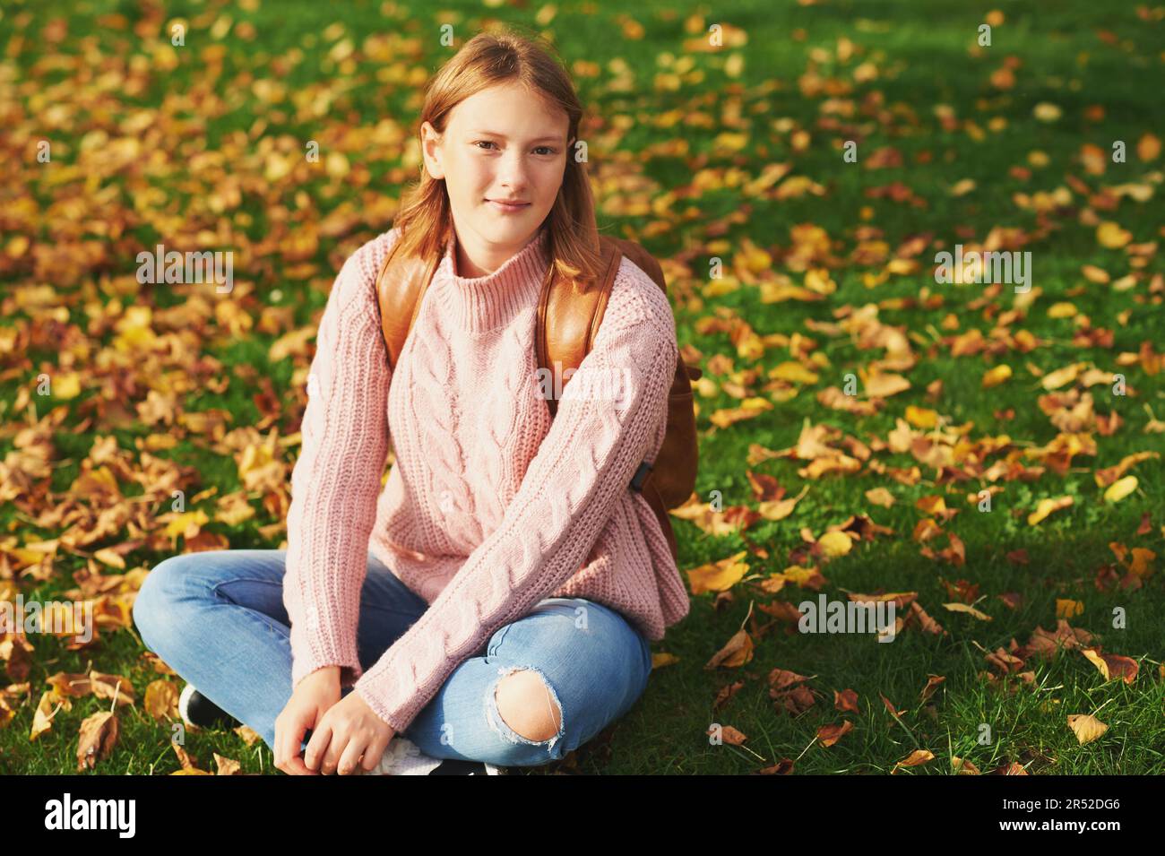 Outdoor portrait of young teenage girl sitting on lawn, wearing ...