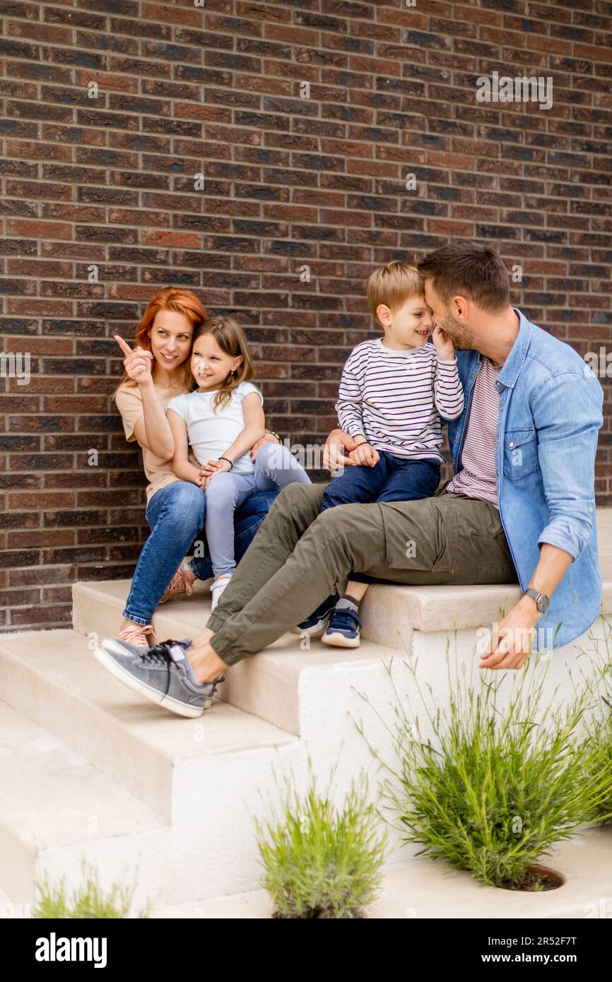 Family with a mother, father, son and daughter sitting outside on steps ...