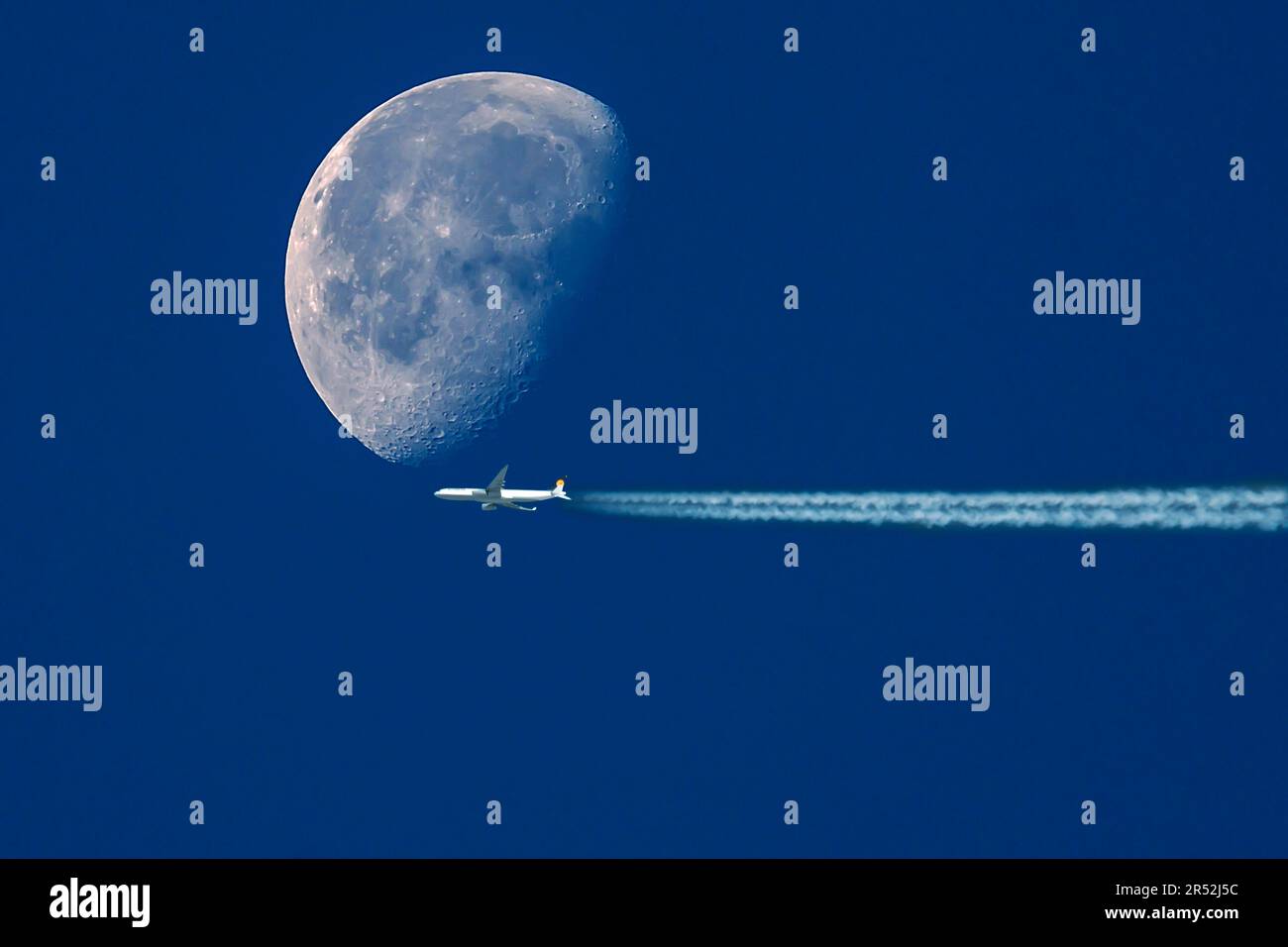 Plane with contrails in front of waning moon in early morning sky ...