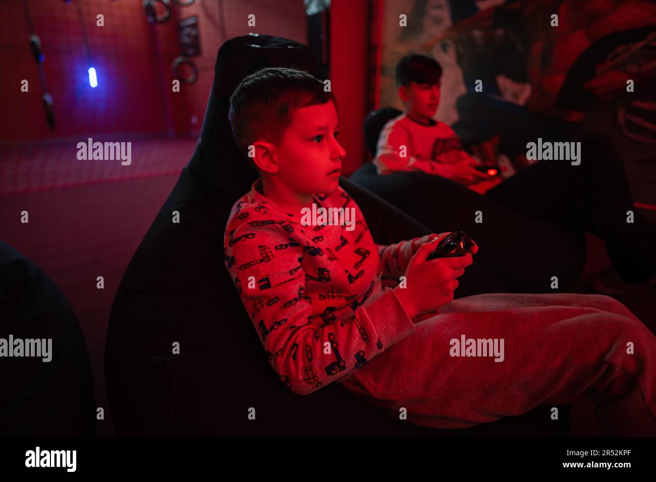 Two boys gamers play gamepad video game console in red gaming room ...