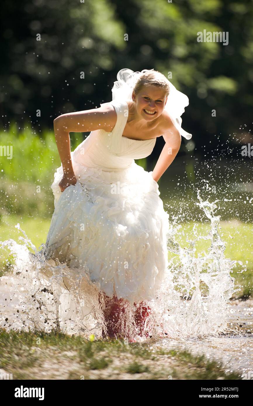 Bride splashes herself wet in small stream with red rubber boots Stock ...
