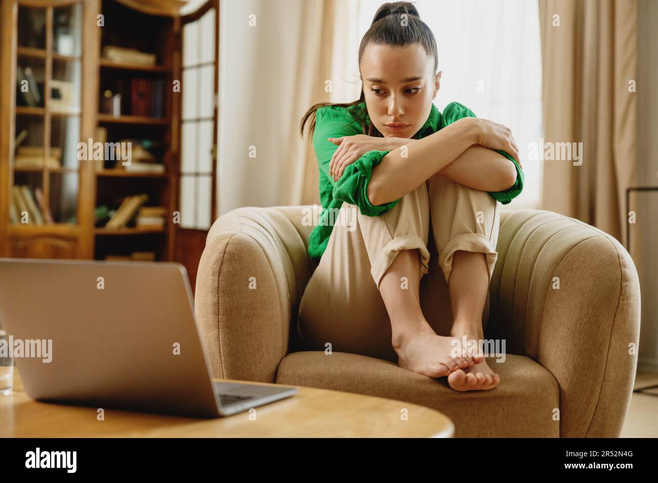 Upset young woman sitting on chair and looking in laptop screen Stock ...
