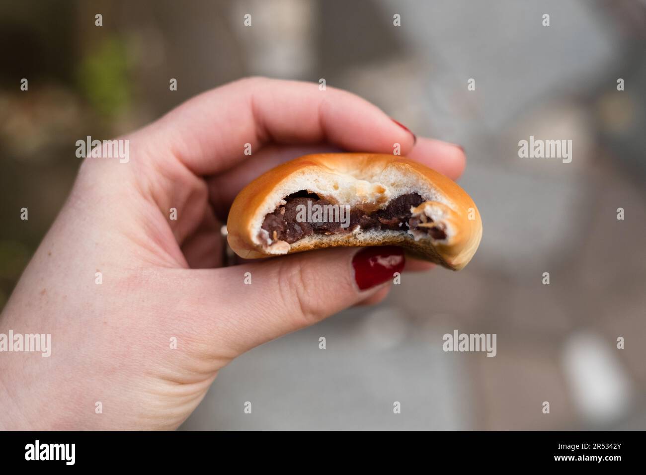 Hand holding a red bean paste bun that has been bitten into, showing ...