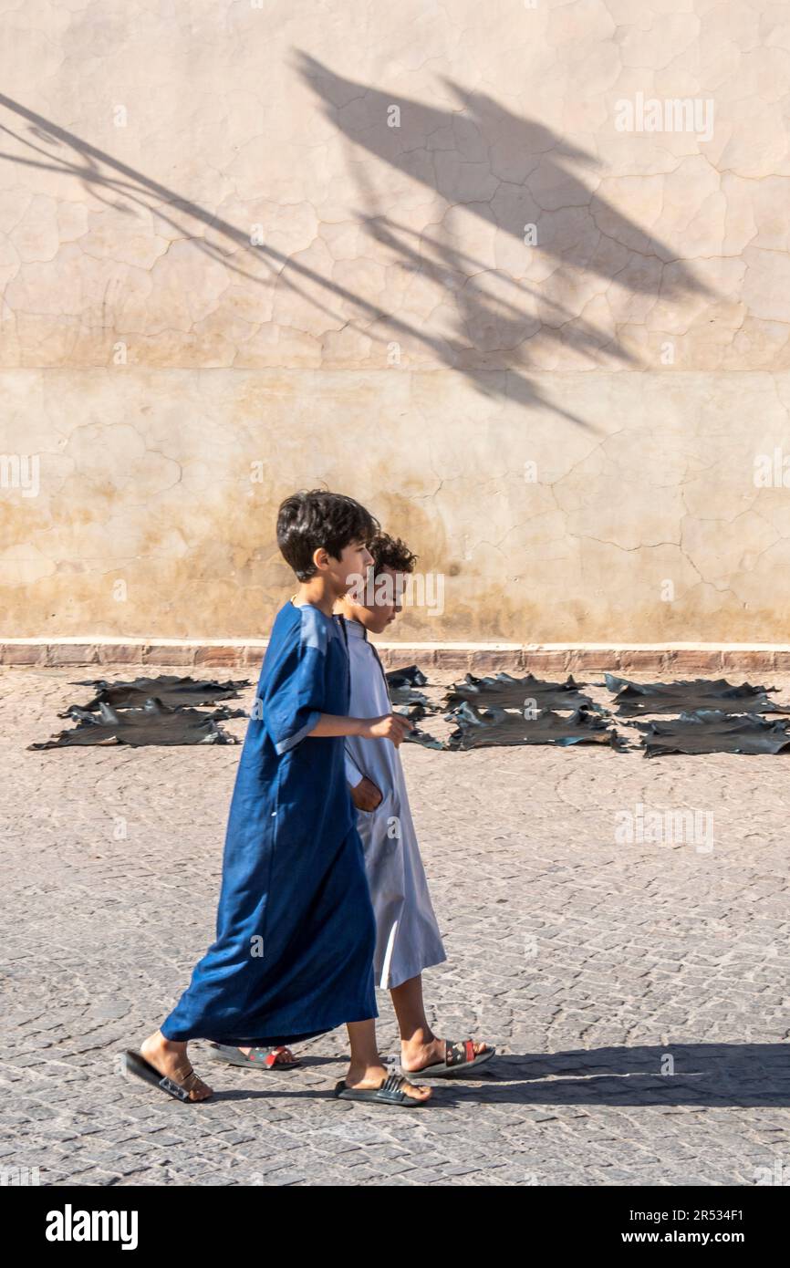 Two young boys walk past drying hides in front of Ben Youssef Mosque ...