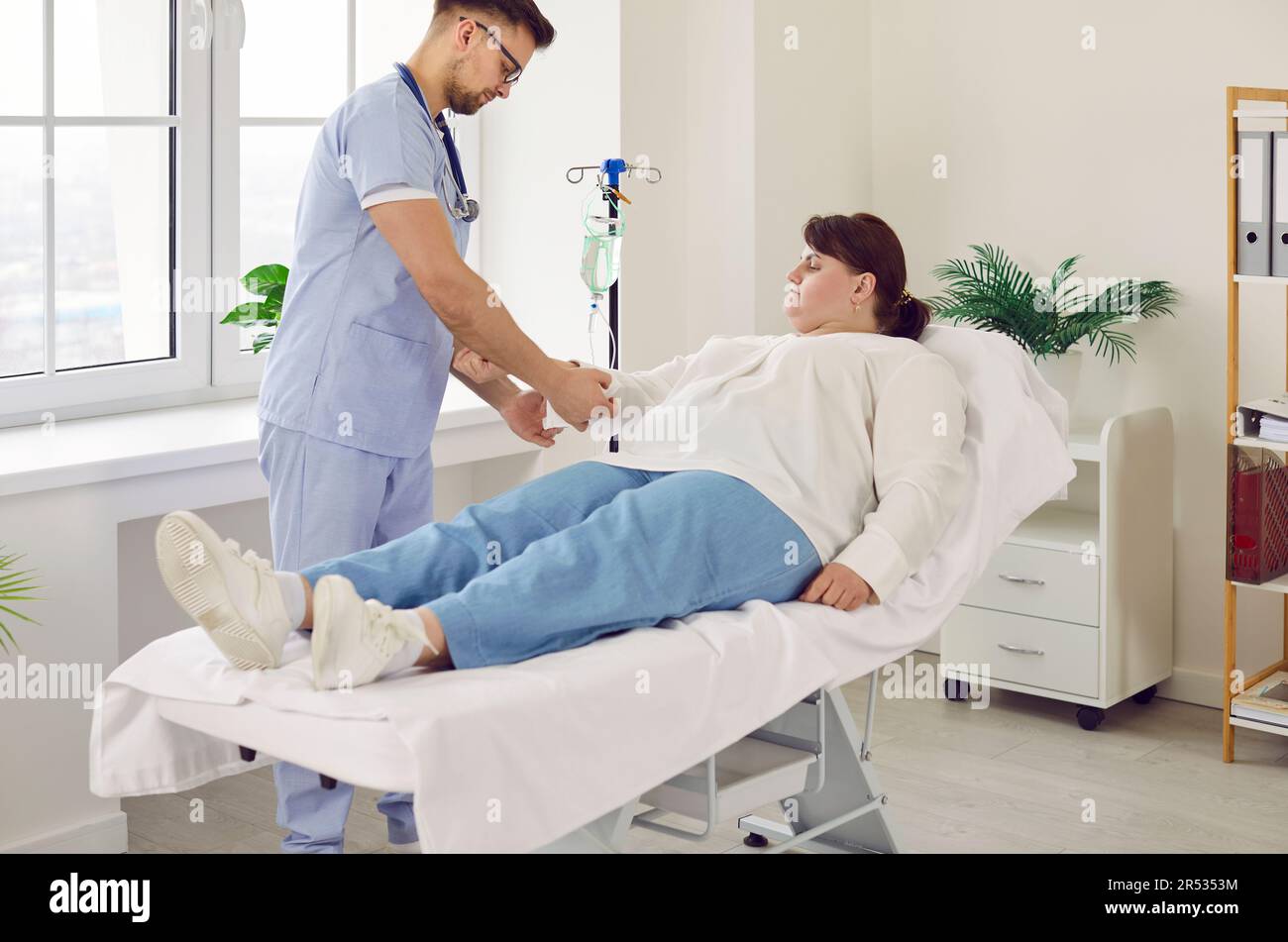 Fat woman lying on the couch in clinic while receiving IV drip infusion ...