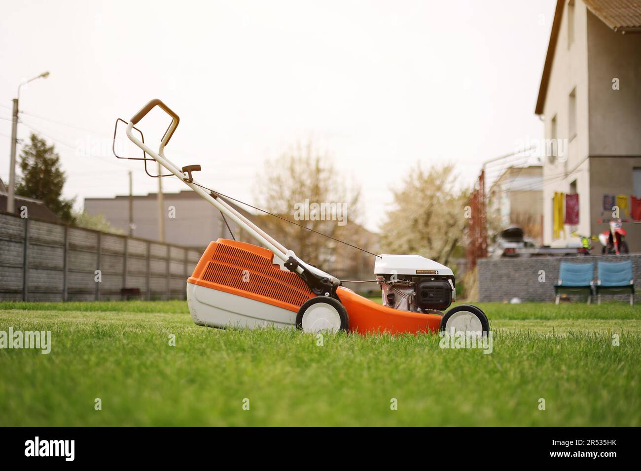 Modern orange-grey electric lawn mower on bright lush green lawn at ...