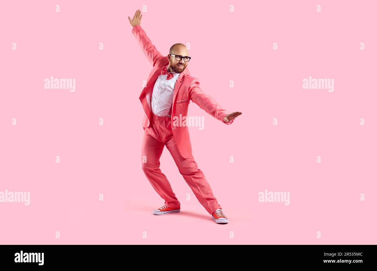 Happy funny guy in a pink party suit, sneakers and glasses dancing in ...
