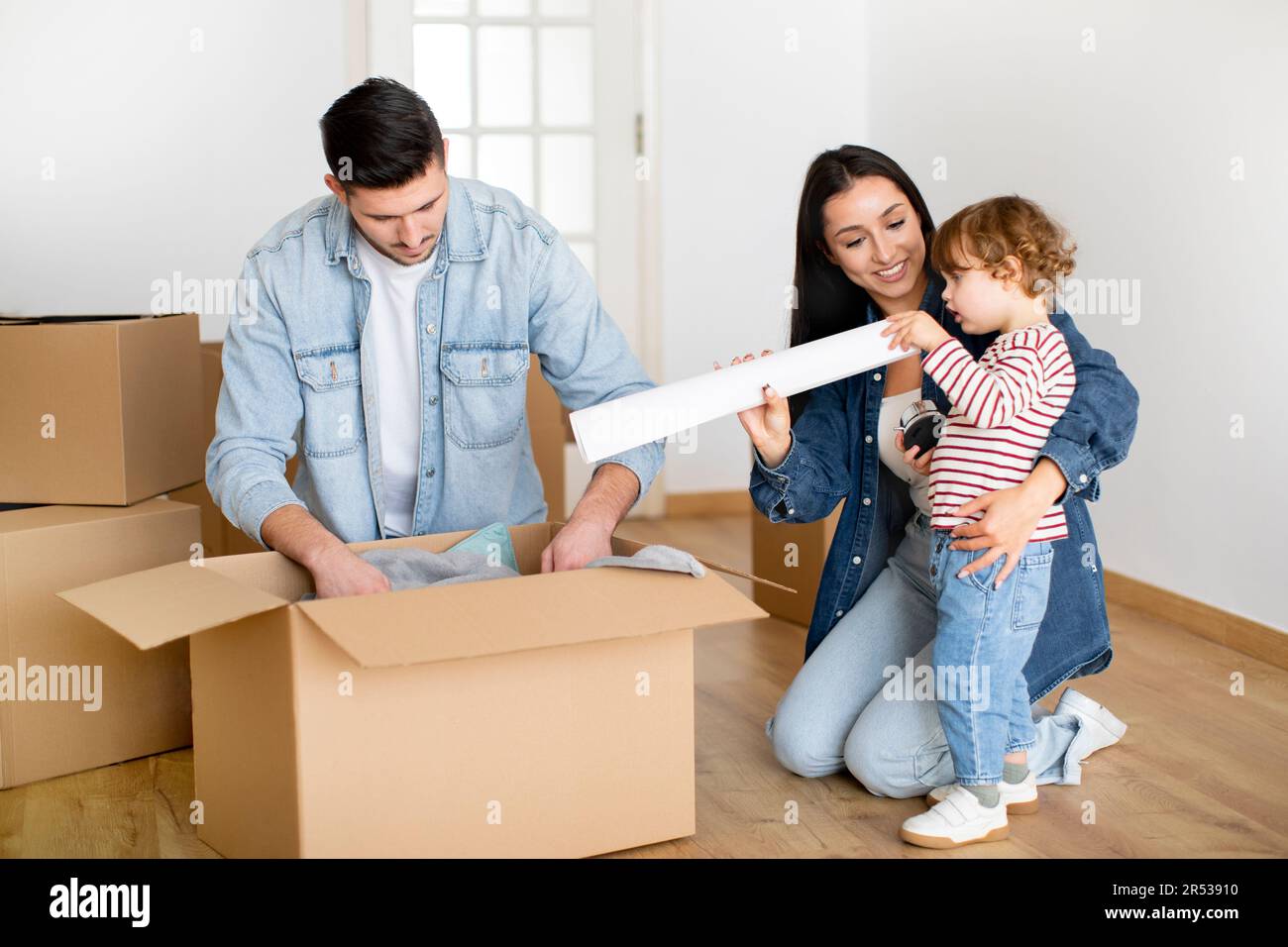 Relocation day concept. Cheerful family of three unpacking belongings ...