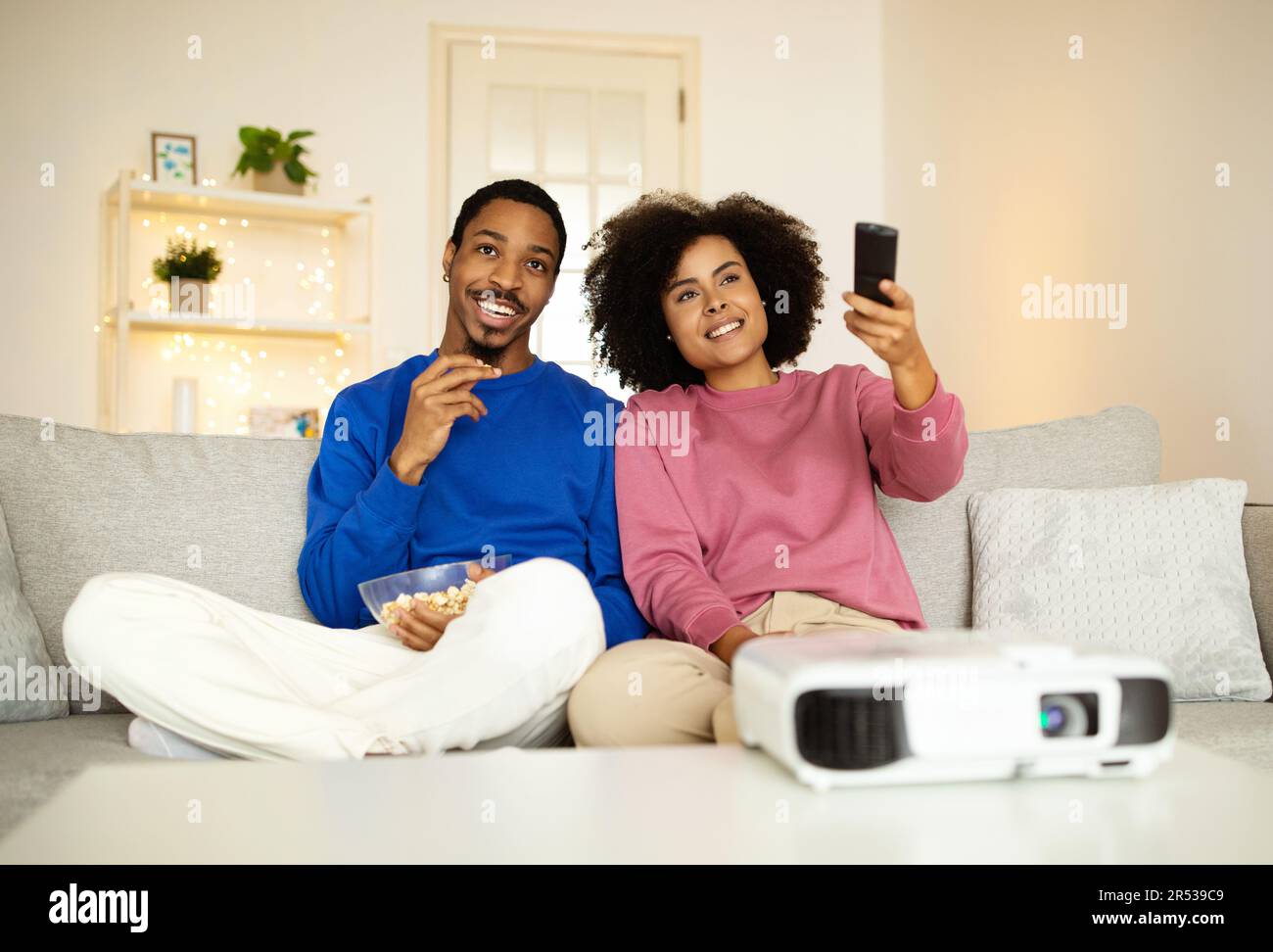 Joyful african couple watching film together using projector at home ...