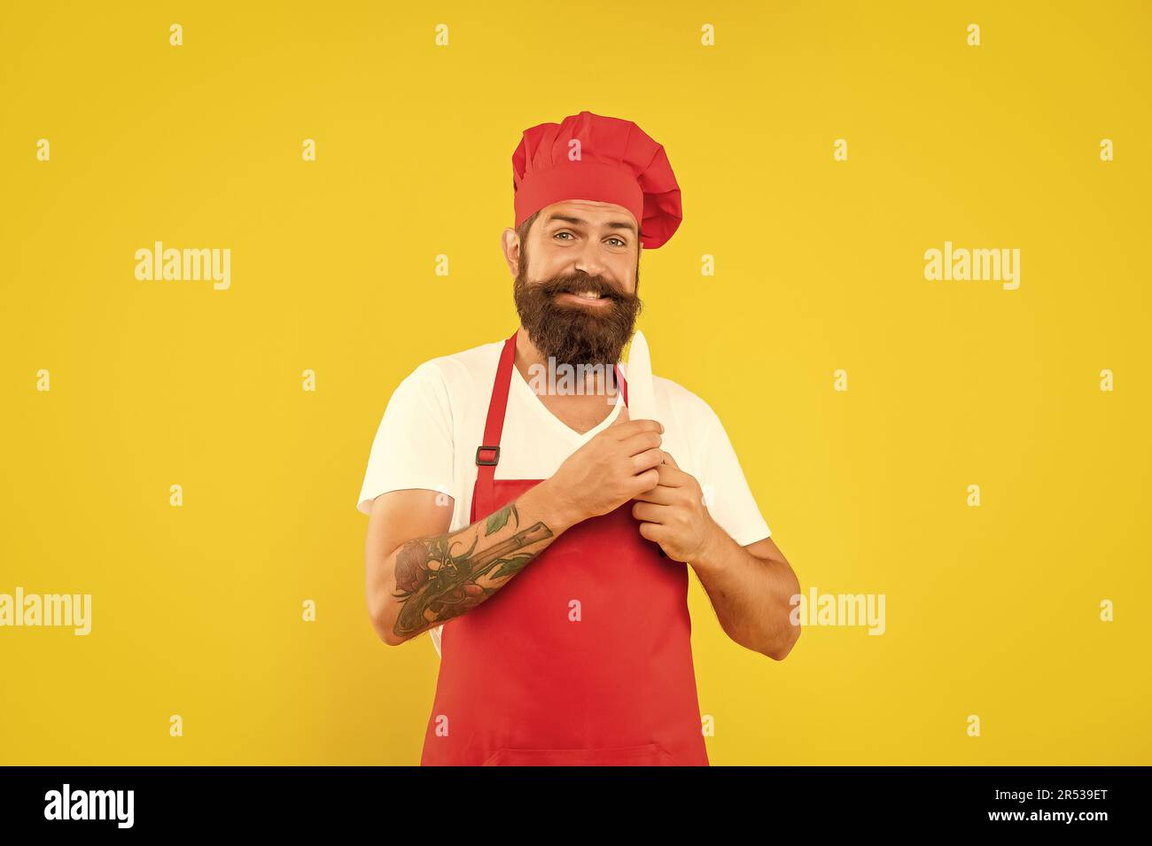Happy man in red apron and toque holding chefs knife yellow background ...