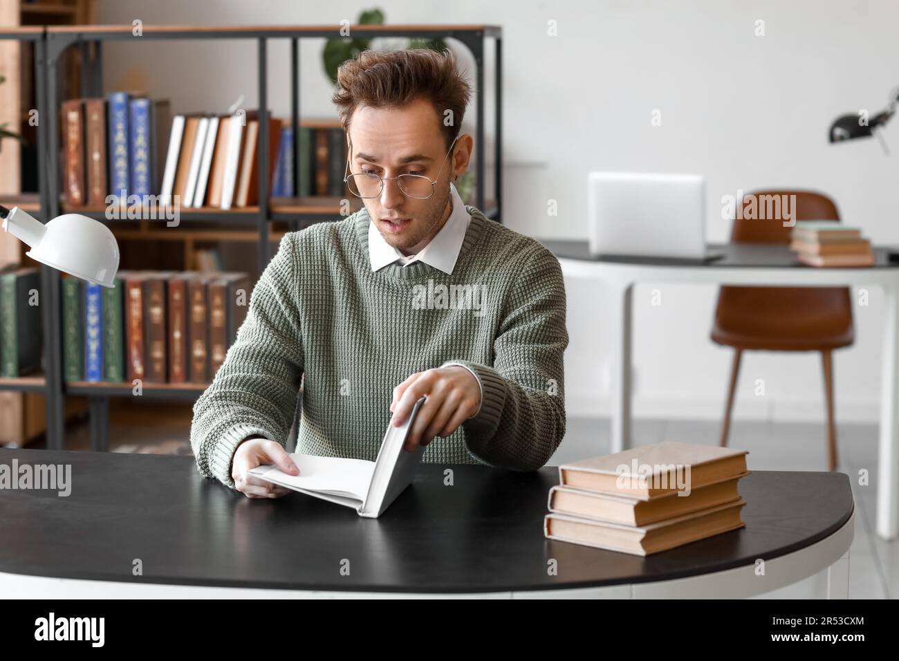 Shocked young man reading book at table in library Stock Photo - Alamy
