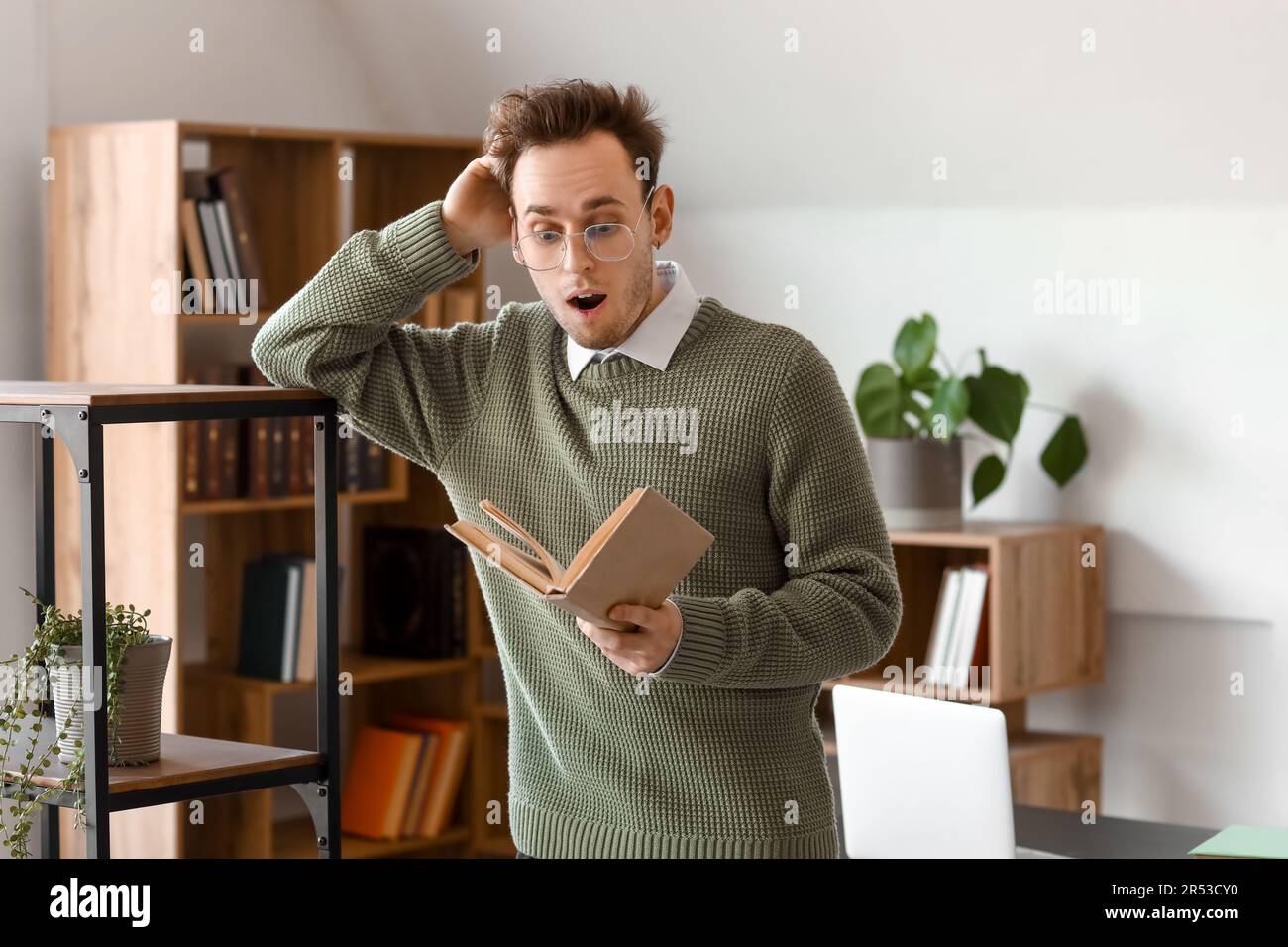 Shocked young man reading book in library Stock Photo - Alamy