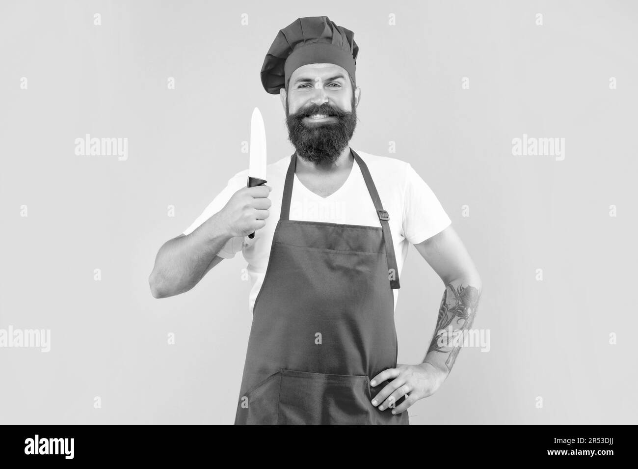 Happy man in red apron and toque holding chefs knife yellow background ...