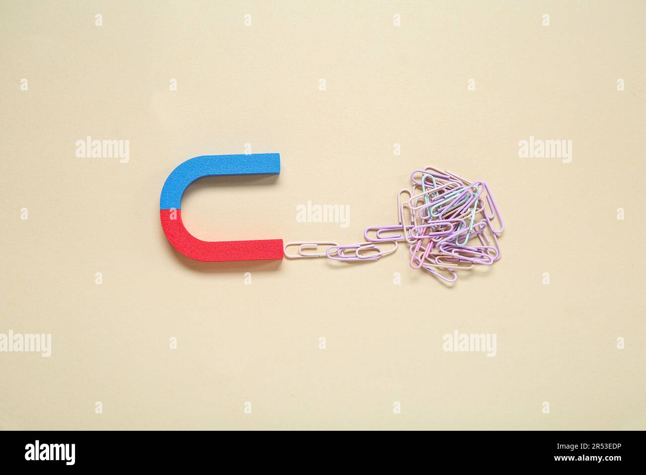 Magnet attracting paper clips on beige background Stock Photo - Alamy