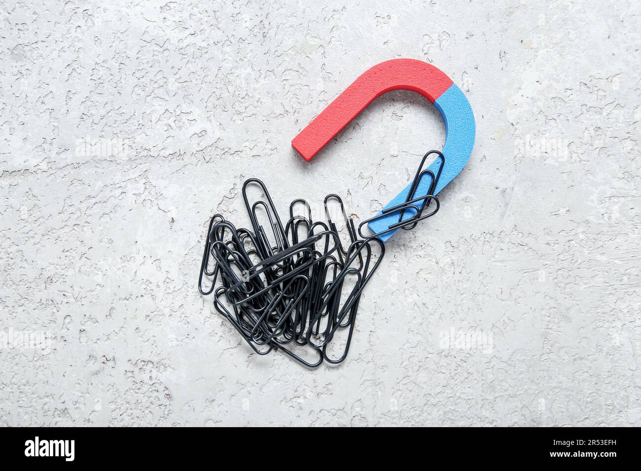 Magnet attracting paper clips on grunge grey background Stock Photo - Alamy