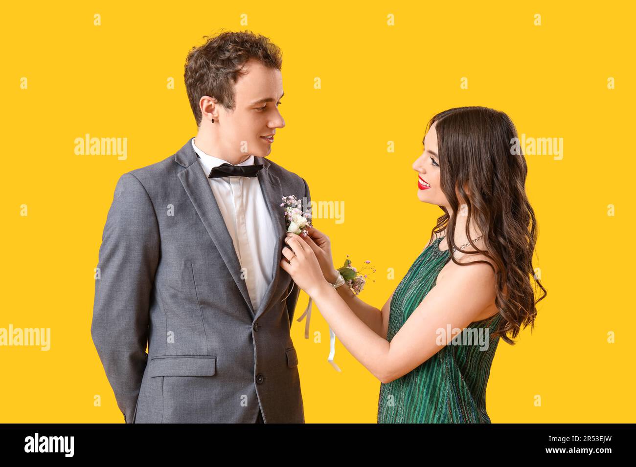 Beautiful prom couple pinning boutonniere on yellow background Stock ...
