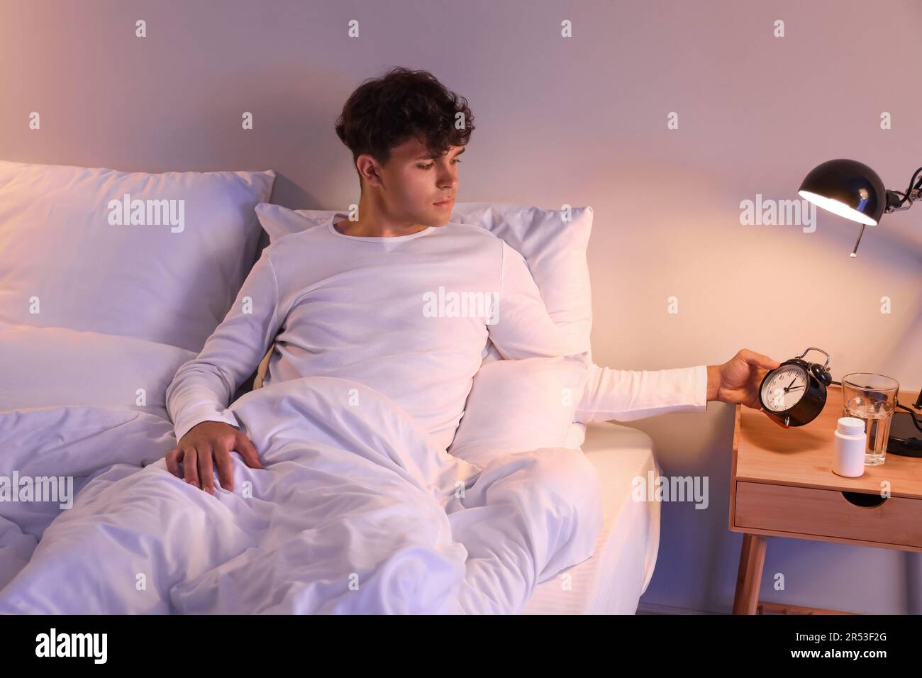 Young man watching time in bed at night Stock Photo - Alamy