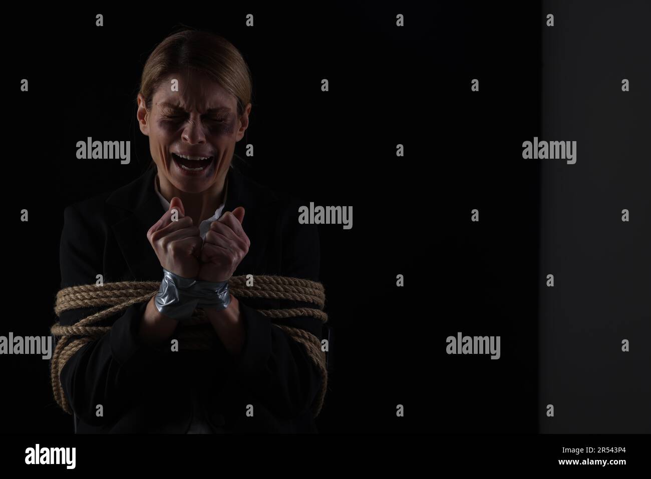 Scared woman tied up and taken hostage on dark background. Space for ...