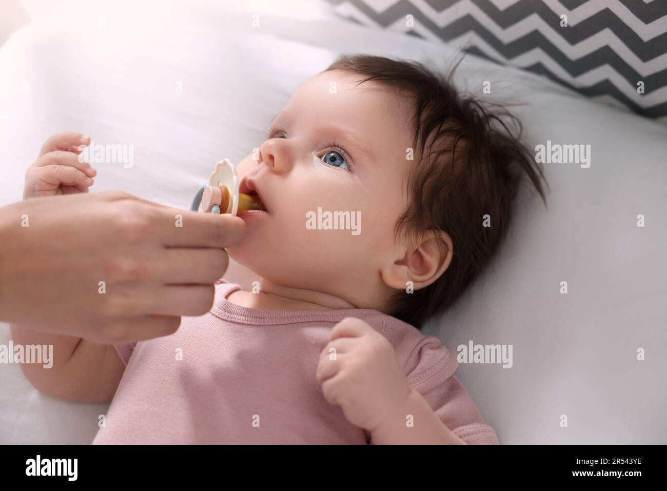 Mother giving pacifier to her little baby on bed, closeup Stock Photo ...