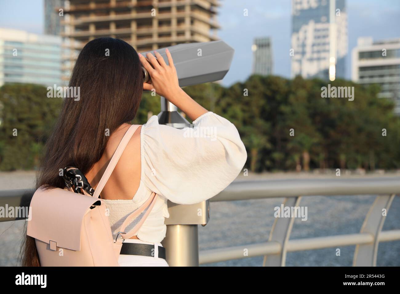 Young woman looking through tourist viewing machine at observation deck ...