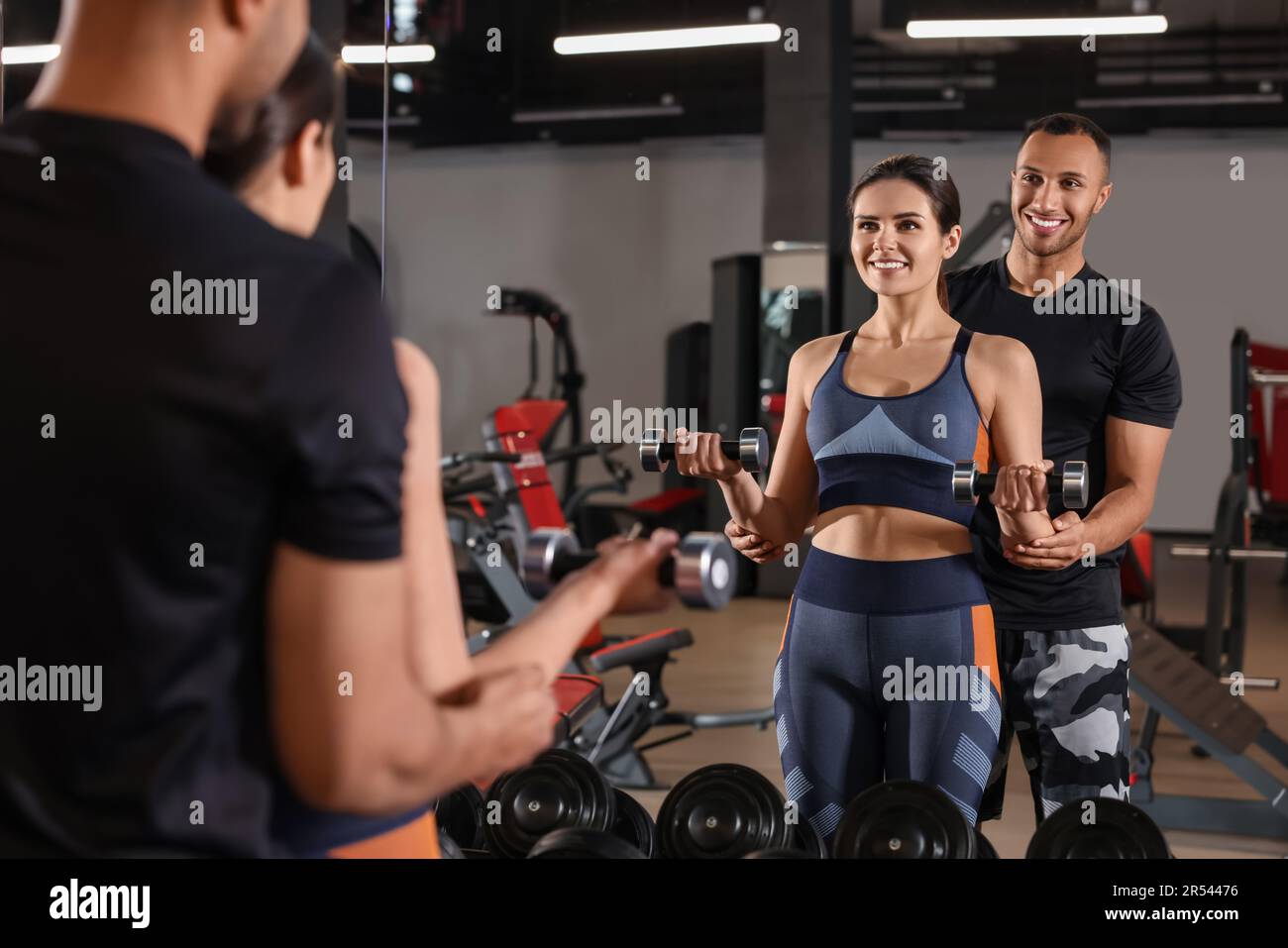 Happy trainer showing woman how to do exercise properly in modern gym ...